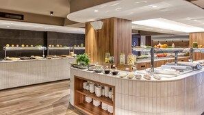 Uma área de buffet com diversas opções de comida, incluindo frutas, saladas e pratos quentes, dispostos em um balcão com detalhes em azulejo e madeira.