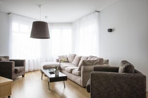 Uma sala de estar com sofá, duas poltronas, uma mesa de centro e um lustre.