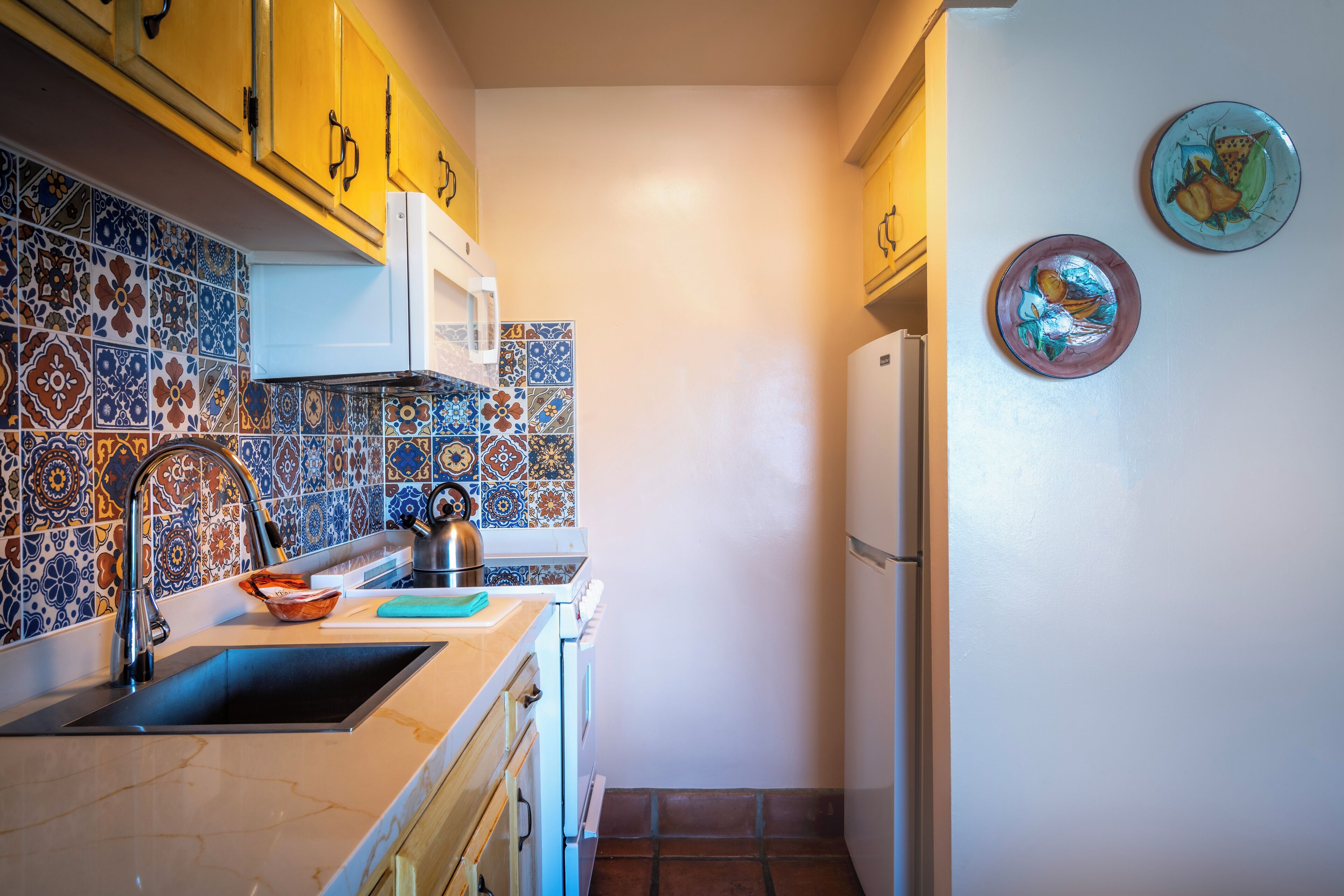 Cozinha estreita com backsplash de azulejos, pia, fogão e geladeira.