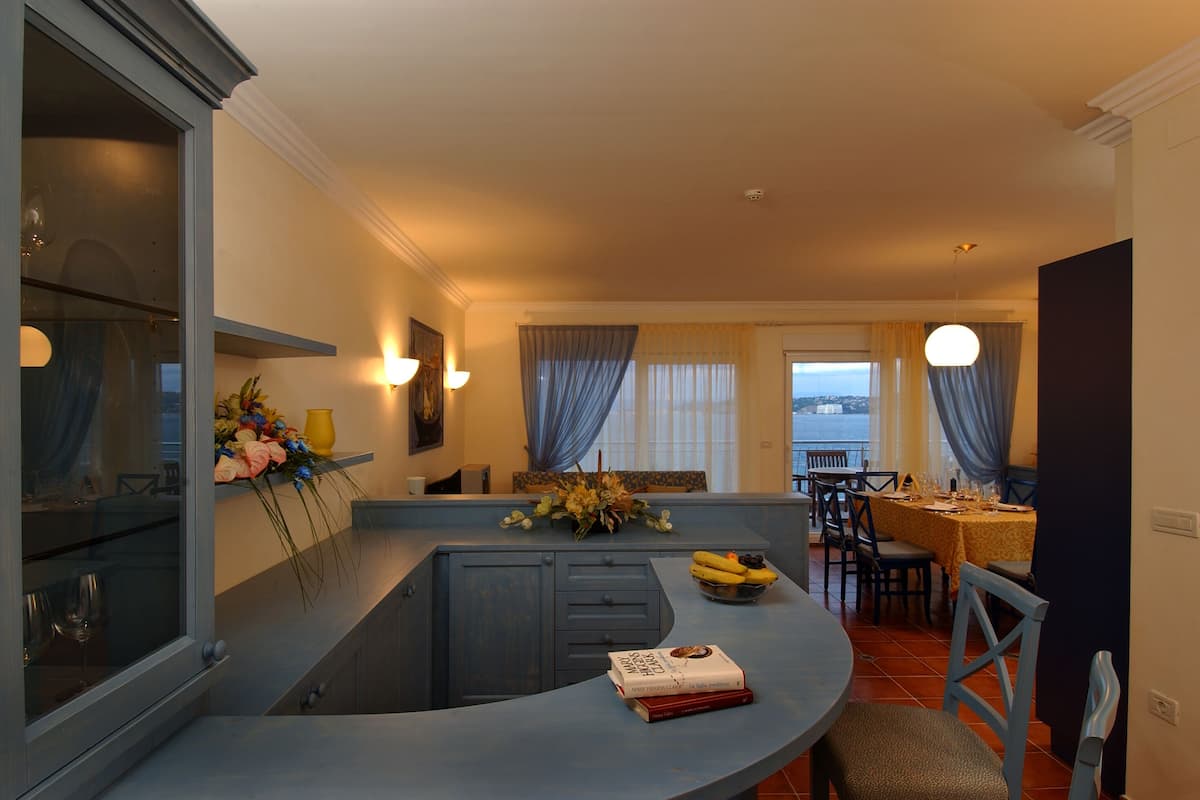 Uma cozinha moderna com bancada curva, área de refeições com mesa posta para dois e vista para o mar pelas janelas.