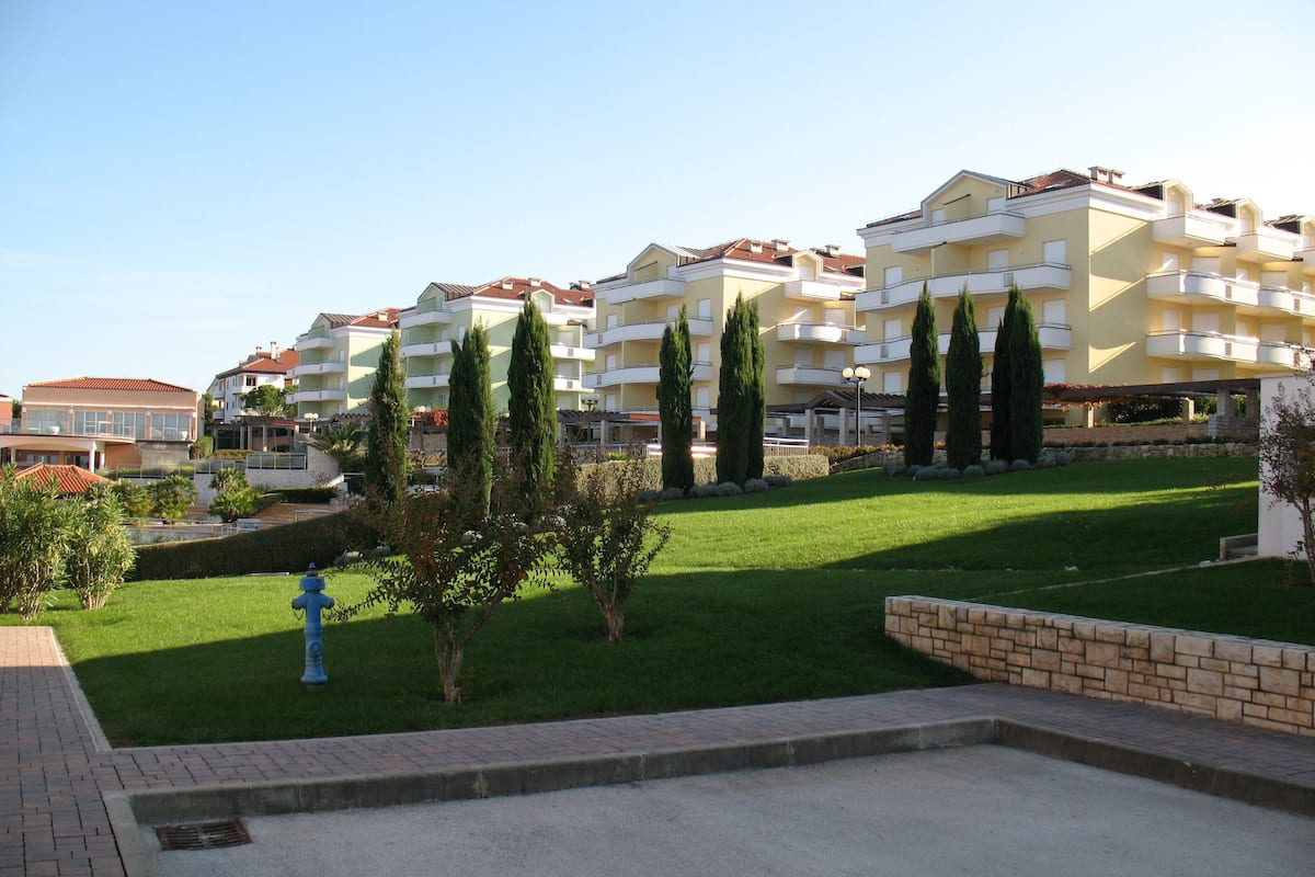 Uma fileira de edifícios de apartamentos modernos com varandas, rodeada por gramados e árvores bem cuidadas.
