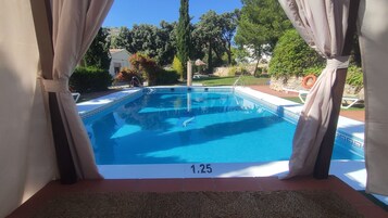 Vista de uma piscina com céu azul e árvores ao fundo.
