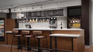 Uma área de bar moderna com bancada branca, banquetas, um quadro de cardápio e uma seleção de vinhos.