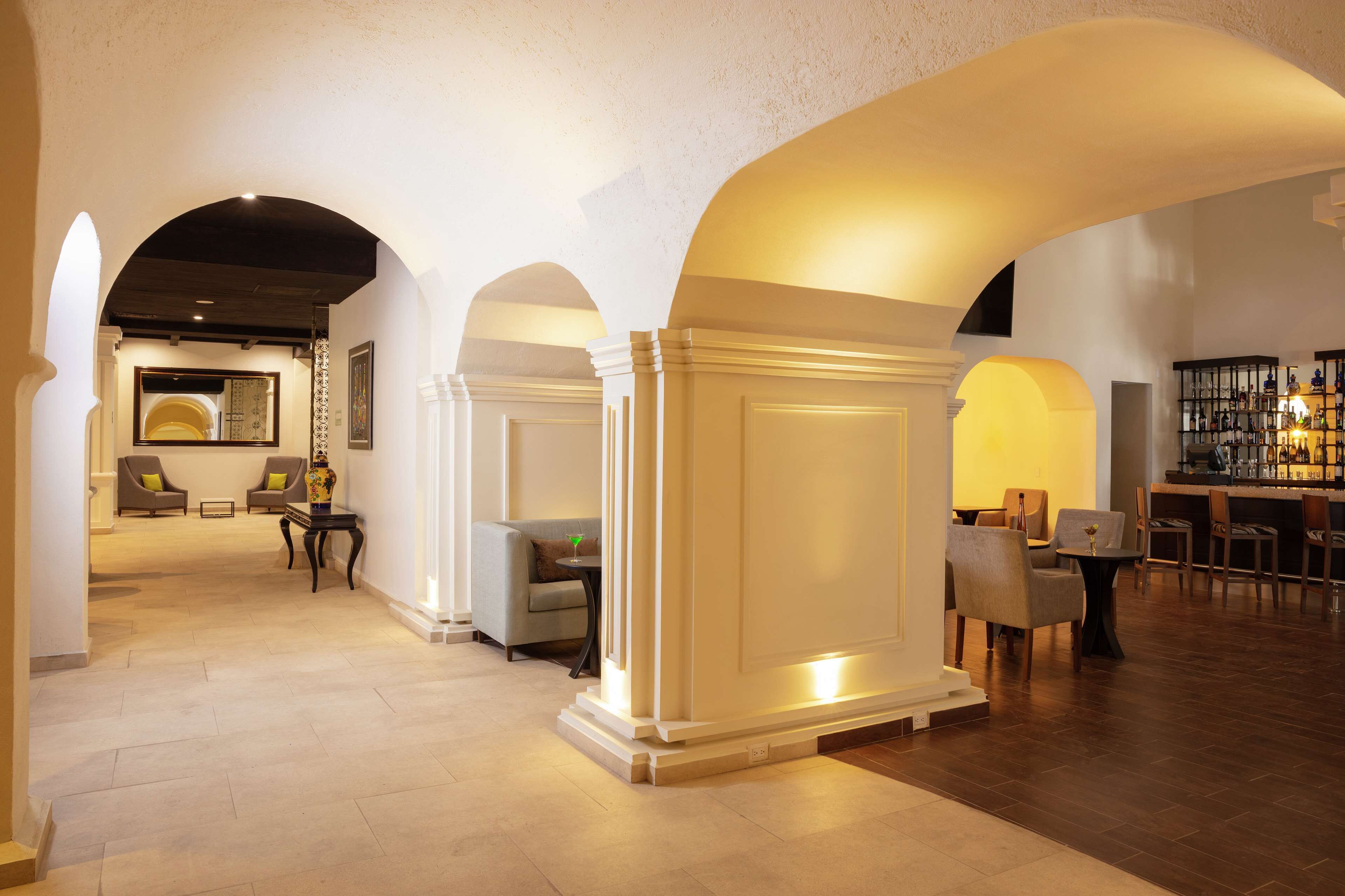 Um hall amplo com tetos altos e arcadas, área de bar com assentos e um balcão de recepção.