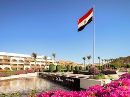 Hotel com bandeira, fonte e jardins bem cuidados.