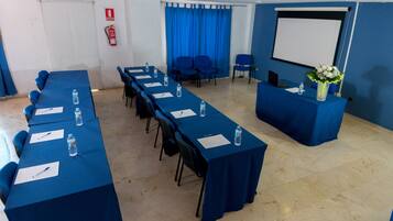 Uma sala de conferências com uma mesa comprida, cadeiras, tela de projetor e extintor de incêndio.