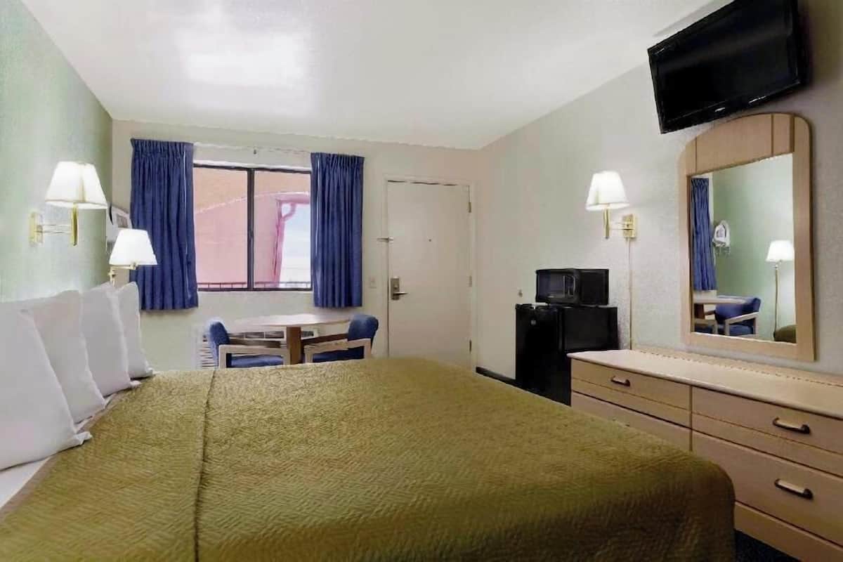 Quarto de hotel com cama, escrivaninha, cadeira, televisão, cômoda e espelho.