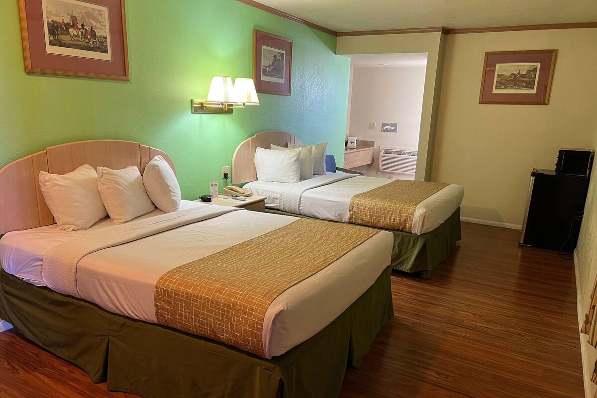 Quarto de hotel com duas camas, paredes verdes e quadros emoldurados.