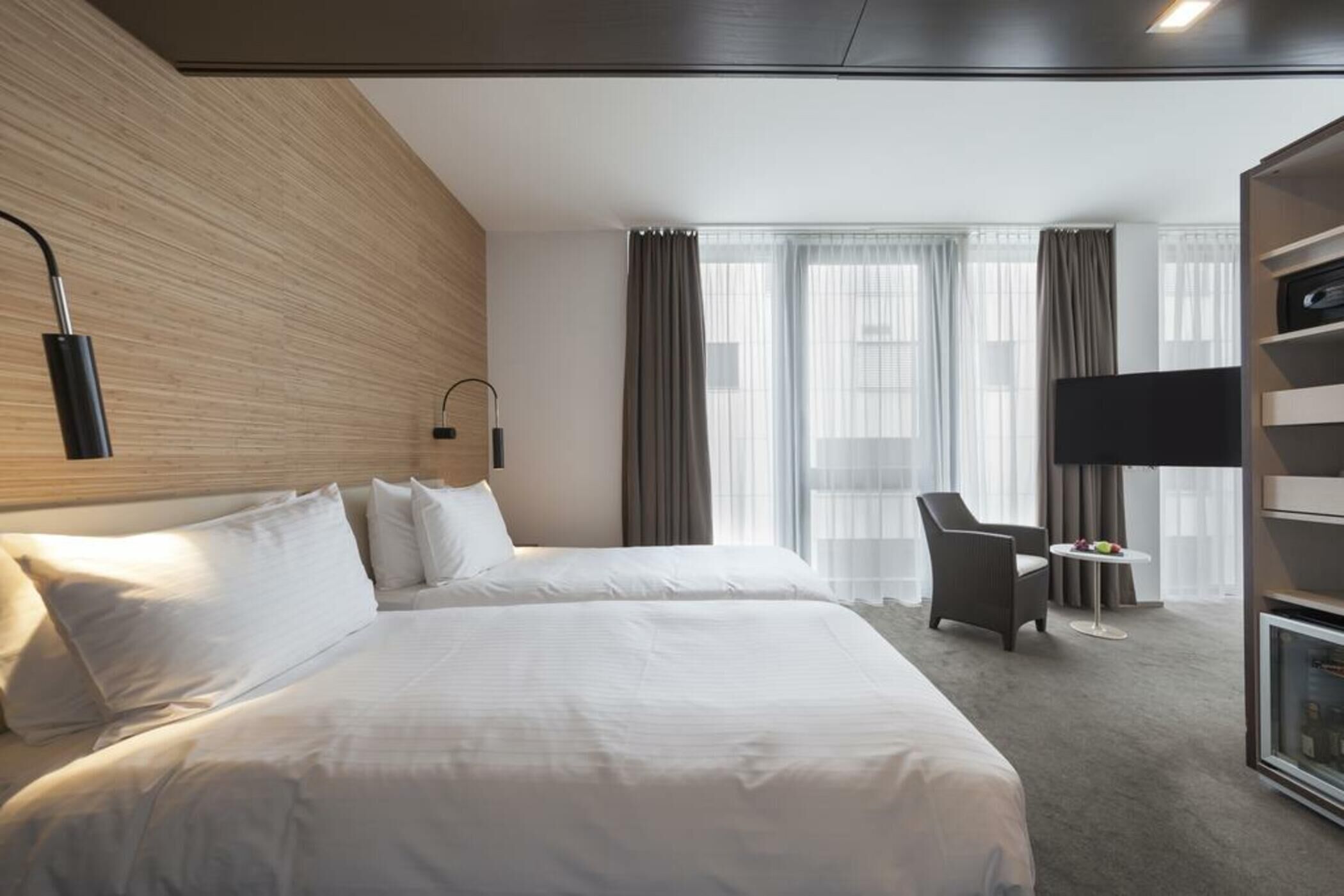 Quarto de hotel com duas camas, televisão, uma cadeira e uma mesinha.