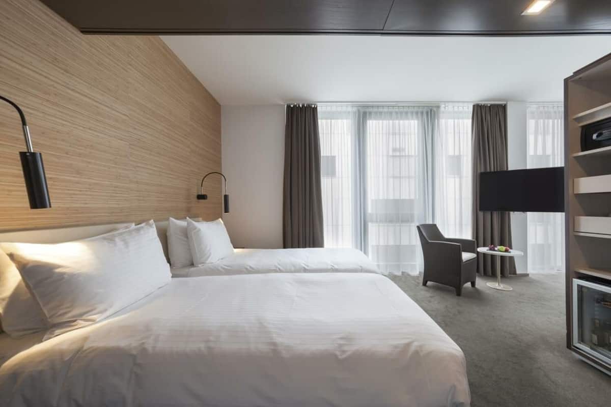 Quarto de hotel com duas camas, televisão, uma cadeira e uma mesinha.