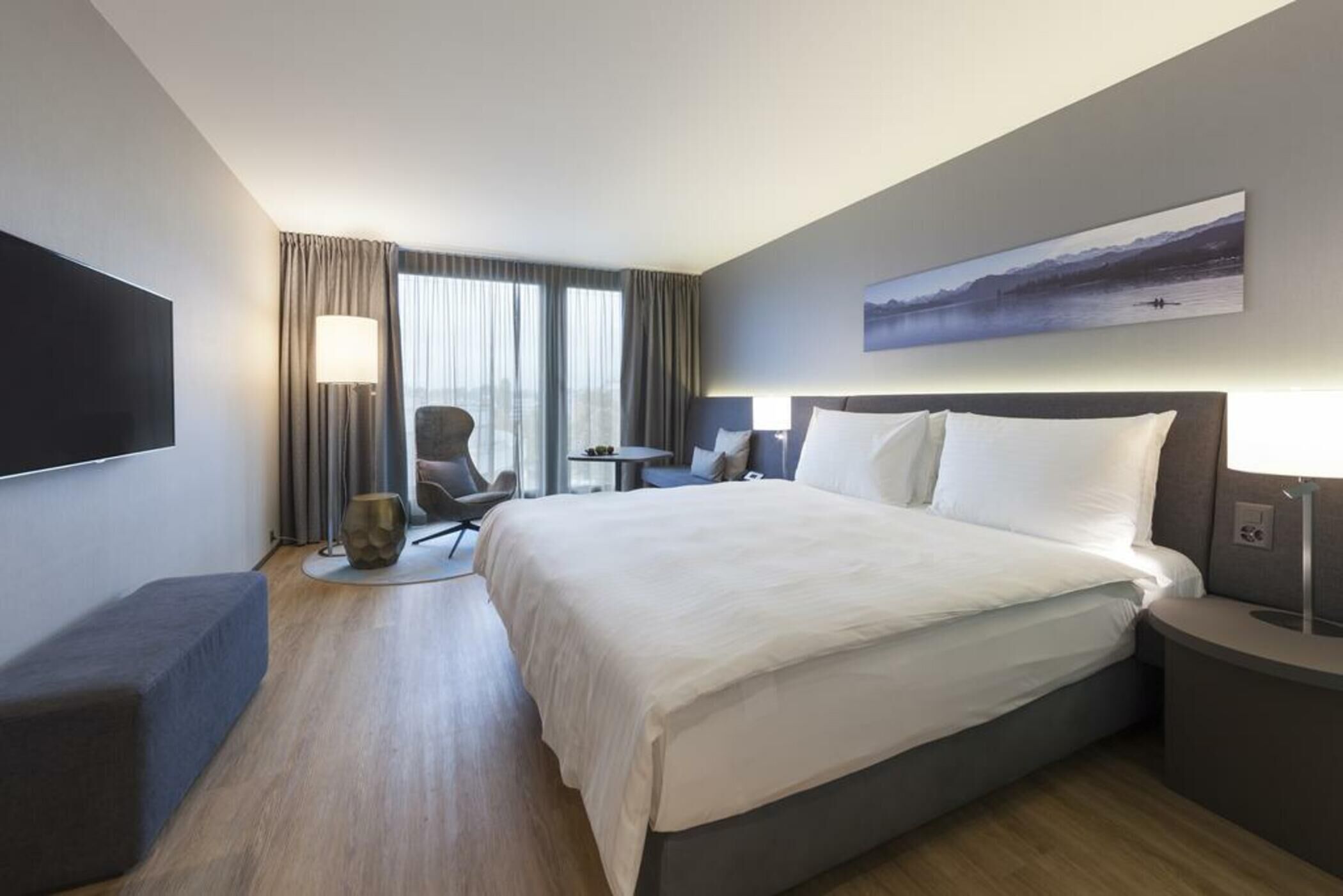 Quarto de hotel com uma cama grande, uma escrivaninha, uma cadeira, uma televisão e um quadro na parede.