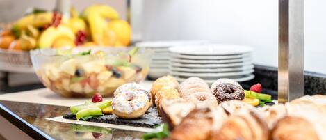 Buffet com diversos alimentos, incluindo frutas, doces e donuts.