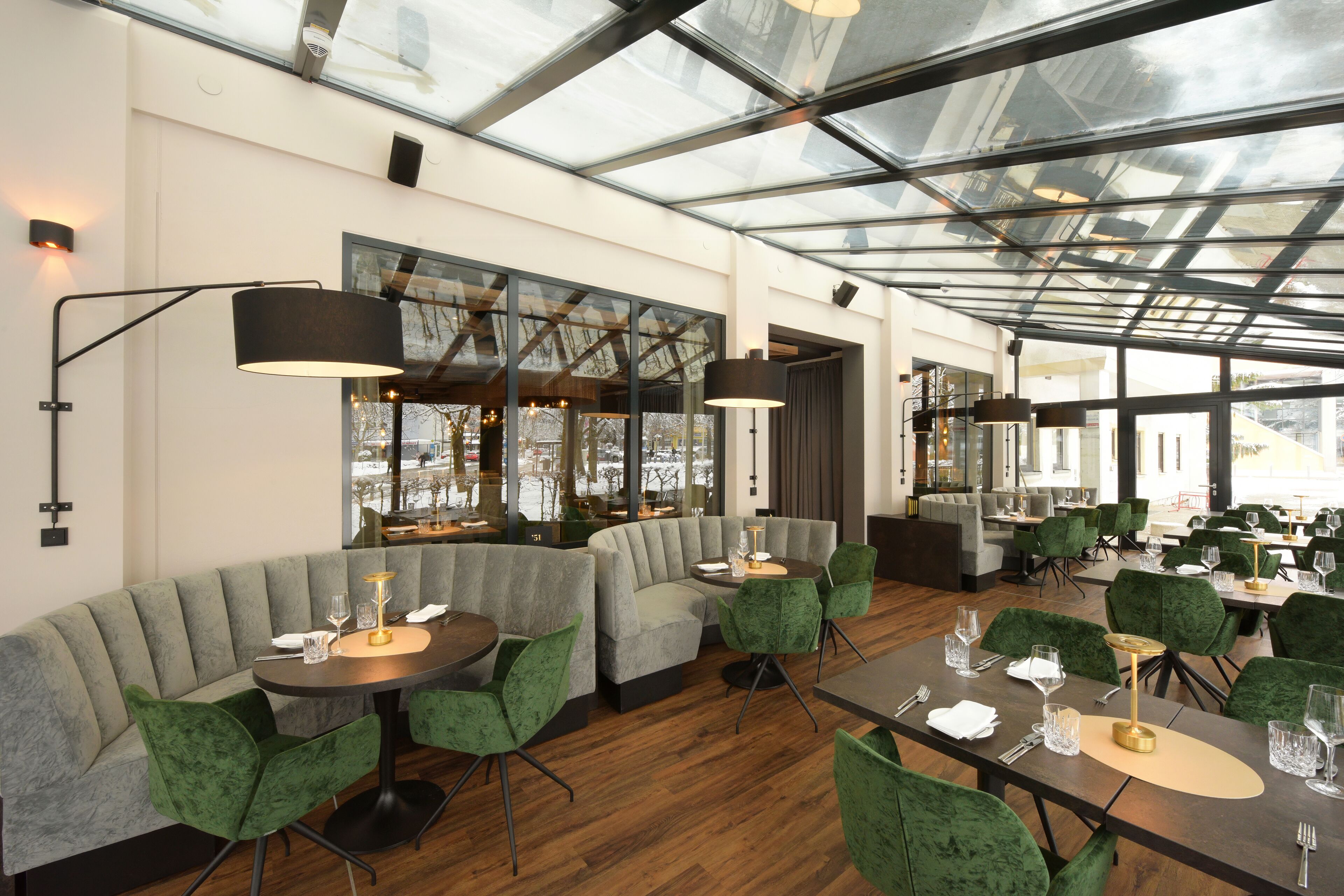 Restaurante moderno com assentos estofados em verde, janelas amplas e teto de vidro.