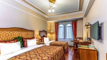 Quarto de hotel com duas camas, uma televisão, uma escrivaninha com luminária e uma janela com cortinas.
