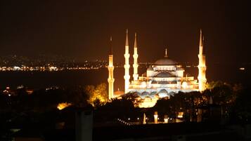 Vista noturna de uma grande mesquita iluminada, com várias minaretes e cúpulas, rodeada por árvores e um corpo d'água.