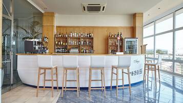 Uma área de bar moderna com balcão curvo, banquetas de madeira e uma grande janela com vista para a cidade.