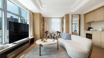 Quarto de hotel moderno com televisão grande, área de refeições e cozinha.