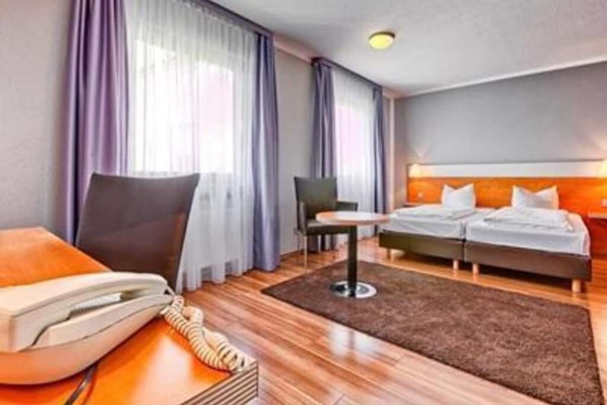 Quarto de hotel com uma cama, uma escrivaninha com telefone, uma cadeira e uma pequena mesa.