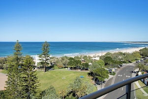 Vista costeira com praia, vegetação e uma estrada com faixas demarcadas.
