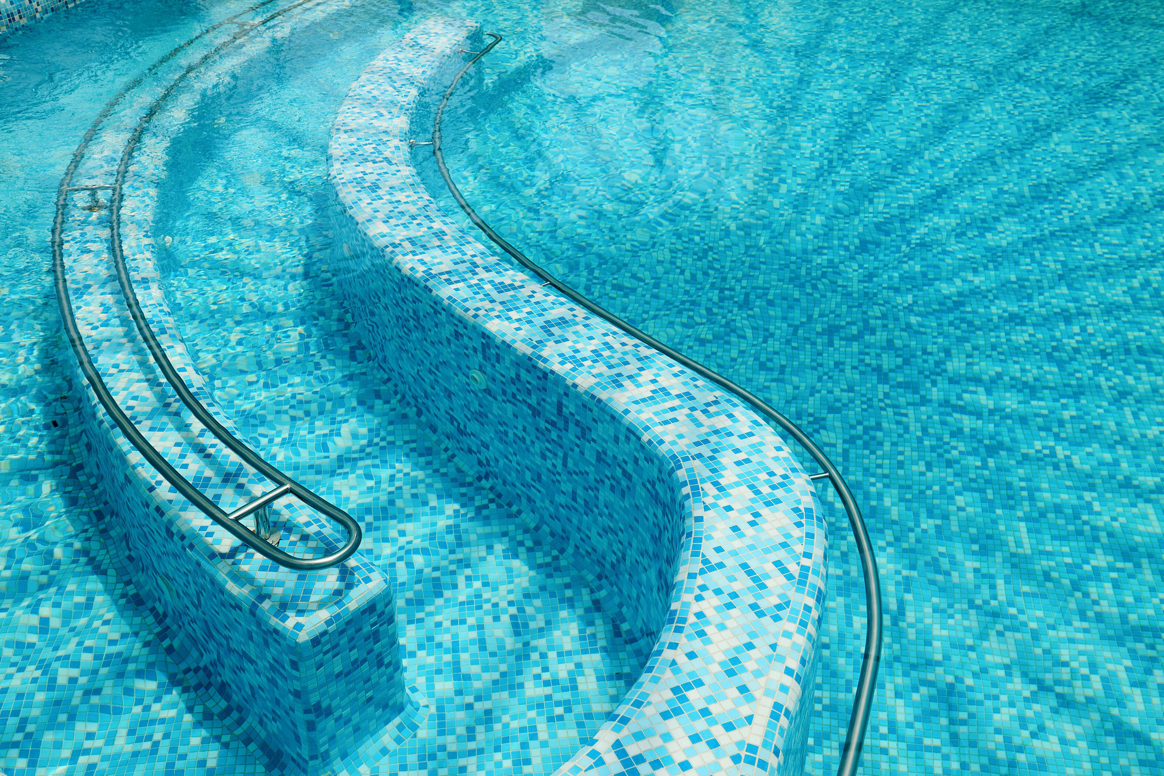 Piscina com borda azulejada e guarda-corpo de metal.