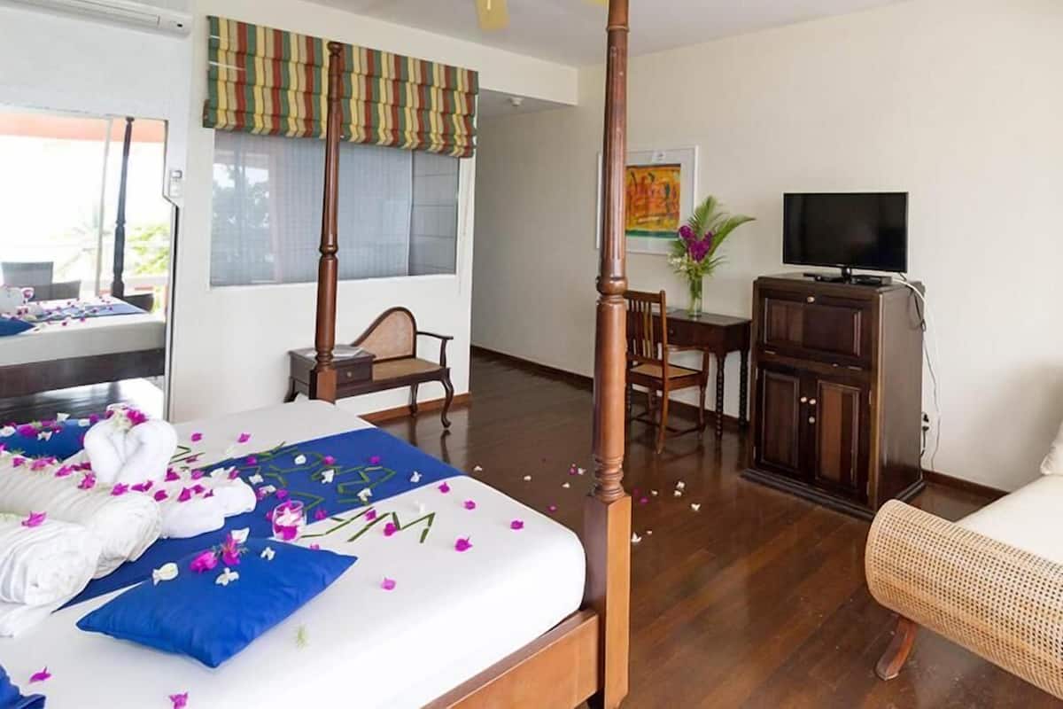Quarto de hotel com cama, escrivaninha, televisão e varanda.