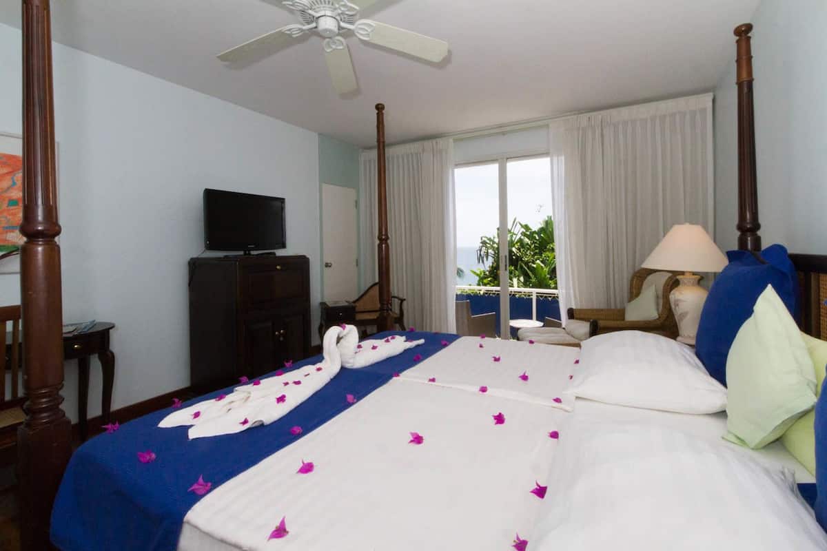 Quarto de hotel com cama, televisão, escrivaninha, cadeira, abajur e vista para o exterior.