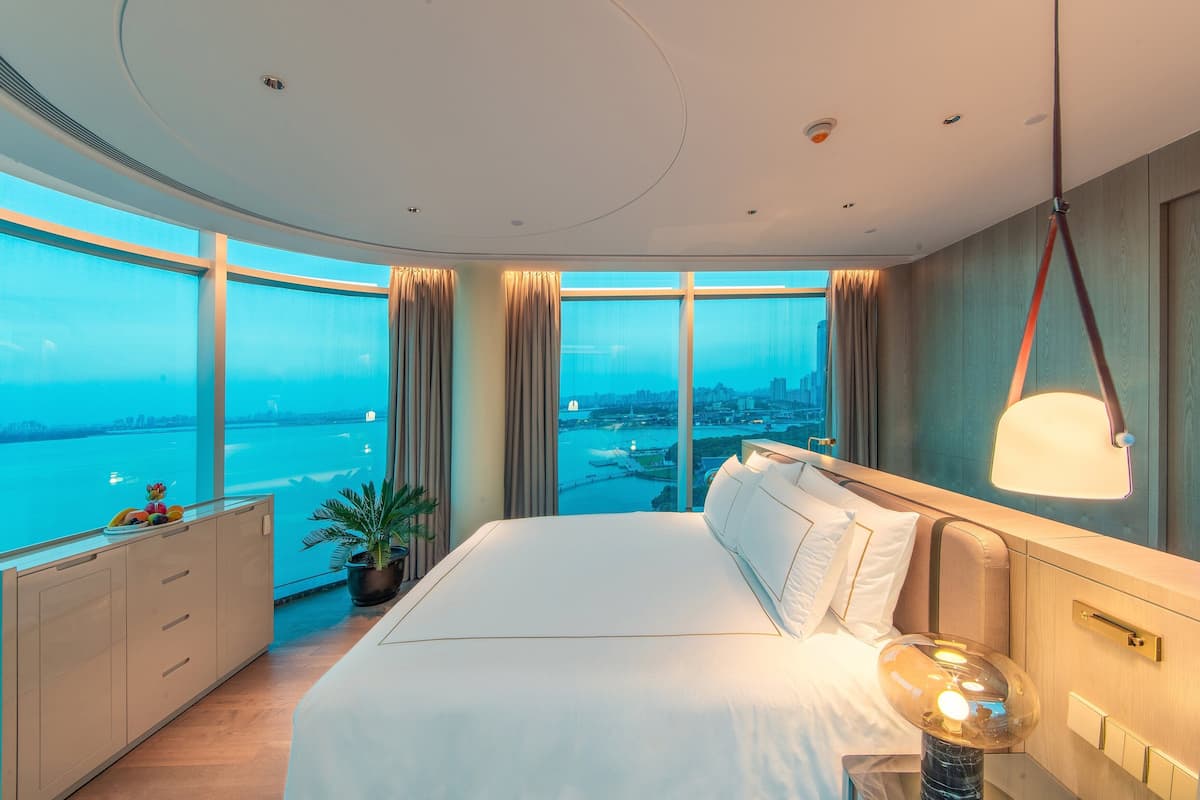 Quarto de hotel moderno com uma cama grande, vista da cidade e varanda com panorama urbano.