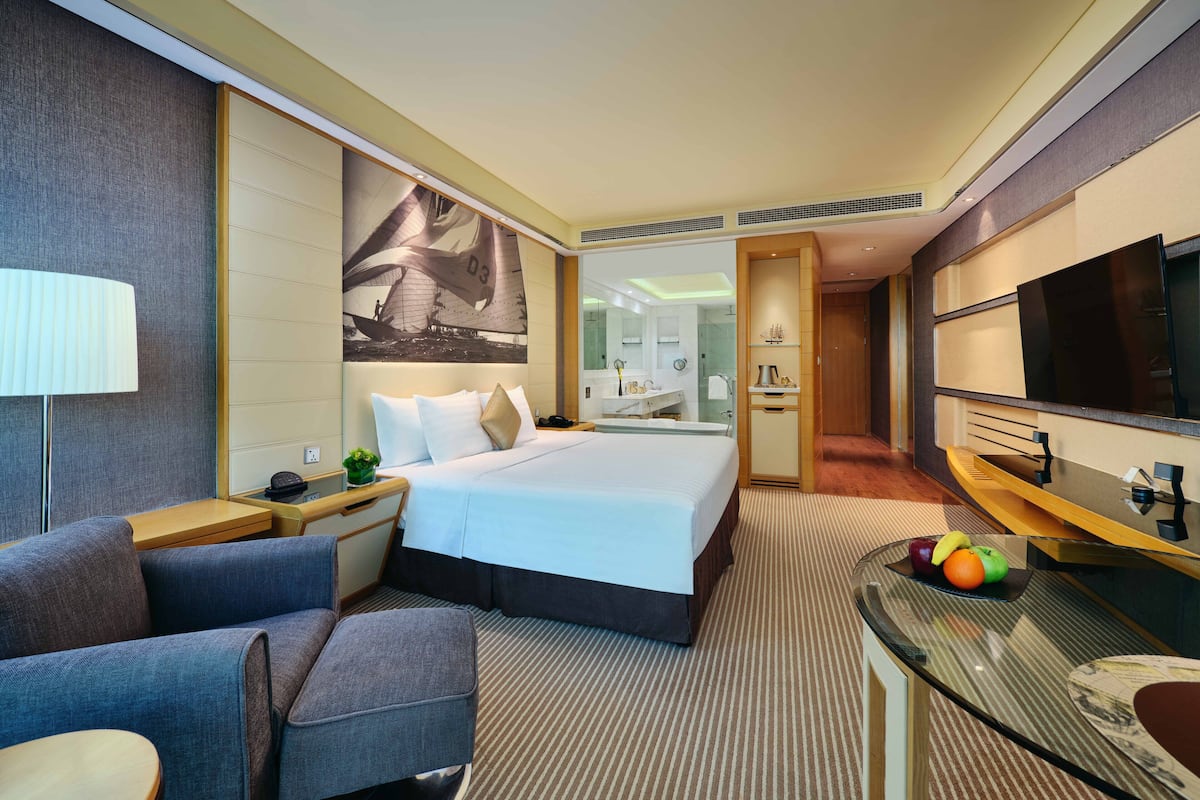 Quarto de hotel moderno com uma cama grande, área de estar, penteadeira com espelho e televisão.