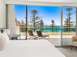Quarto de hotel com uma grande porta de vidro deslizante que dá para uma varanda com vista para o oceano e árvores.