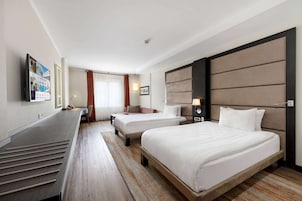 Quarto de hotel com duas camas, uma escrivaninha, televisão e uma janela grande com cortinas.