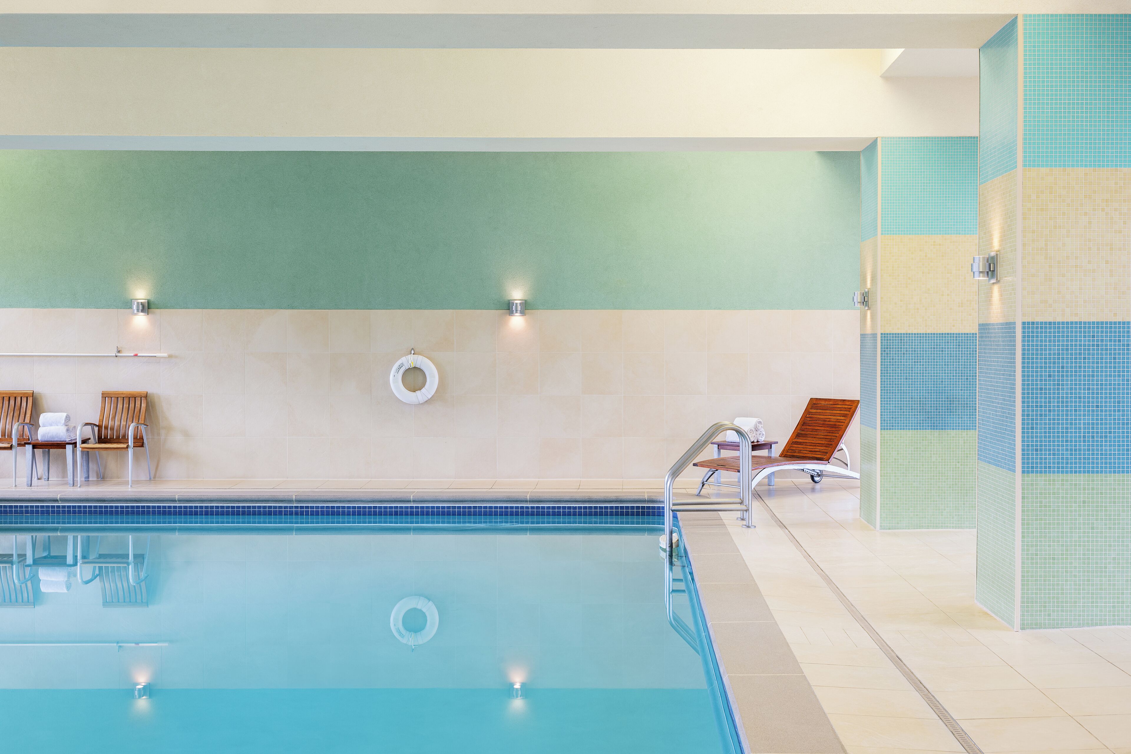 Piscina com espreguiçadeiras e parede revestida em azulejo.