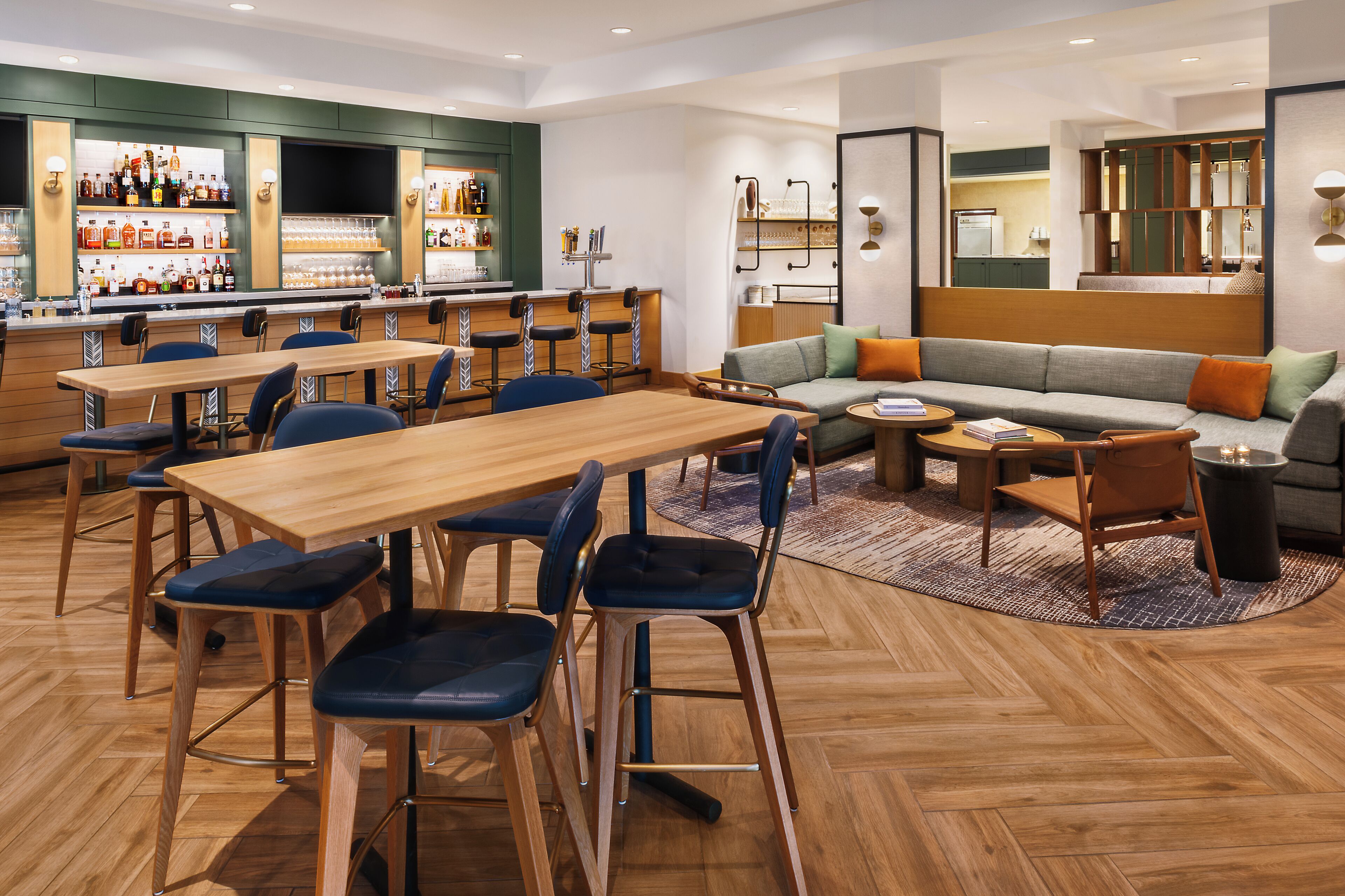 Uma área de bar moderna com móveis de madeira, um sofá e uma cozinha ao fundo.