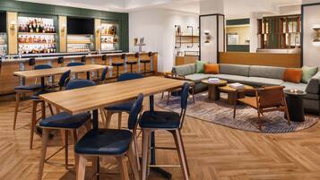 Uma área de bar moderna com móveis de madeira, um sofá e uma cozinha ao fundo.