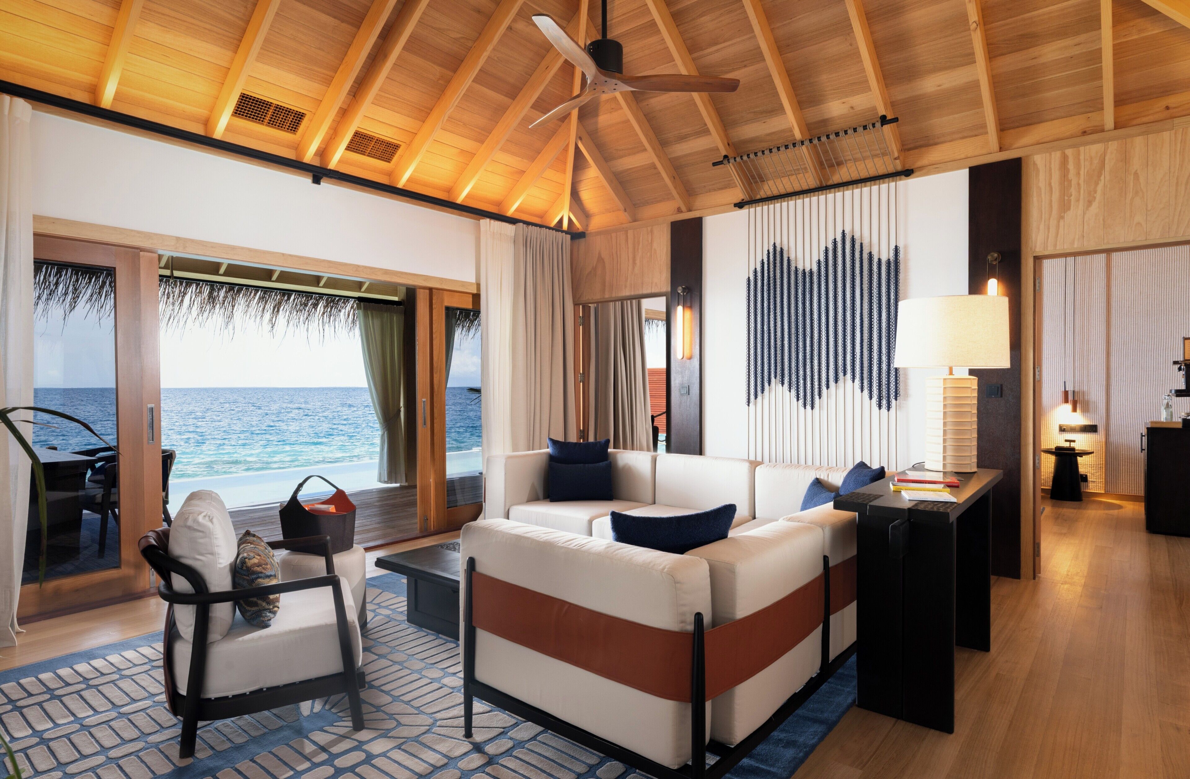 Quarto espaçoso com grande janela com vista para o mar, um sofá, uma mesa de jantar e um ventilador de teto.