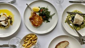 Uma mesa posta com diversos pratos, incluindo peixe, salada e uma sopa verde, juntamente com copos de vinho e talheres.