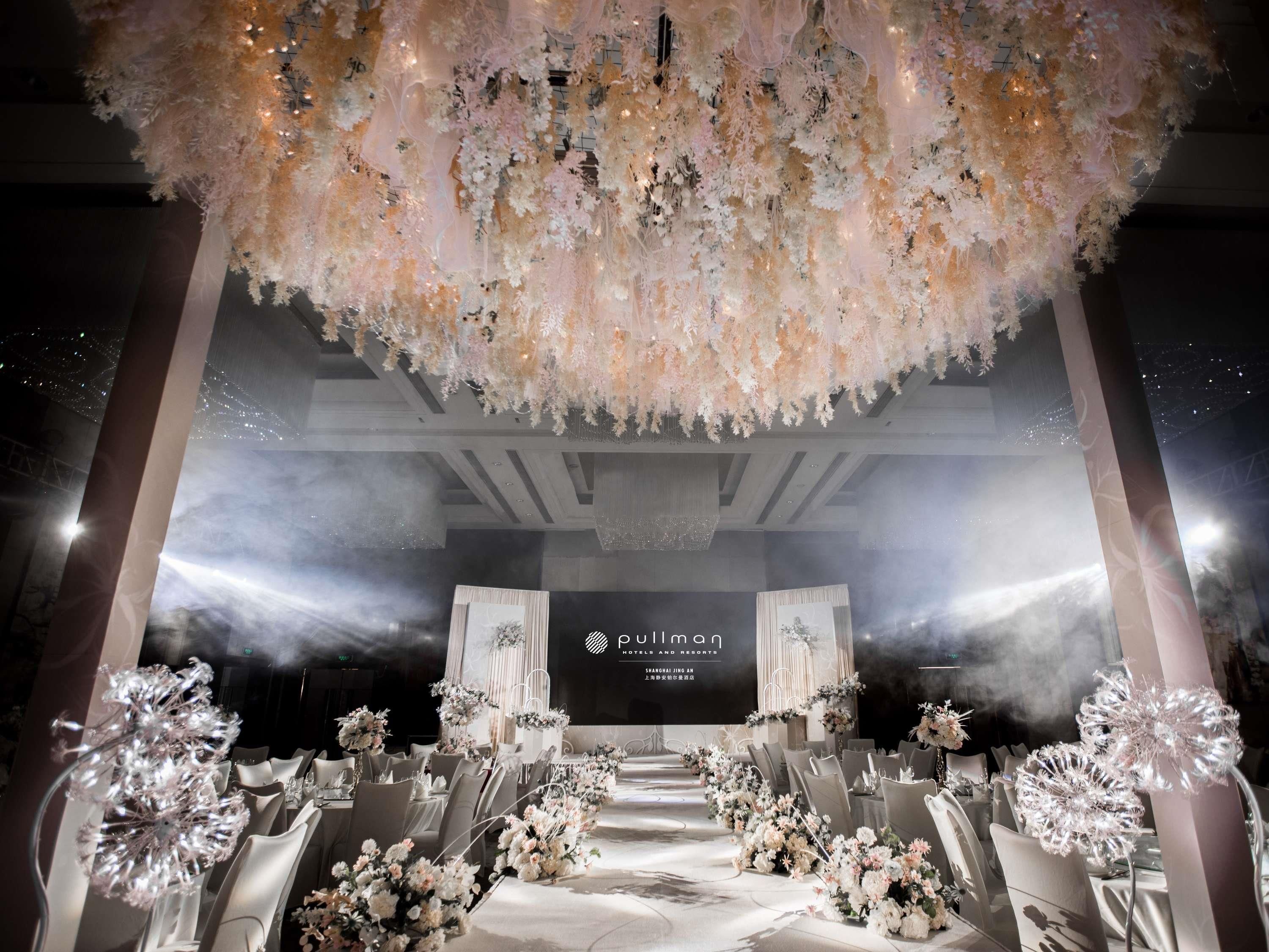 Salão de banquetes com assentos em níveis, centros de mesa florais e um candelabro.