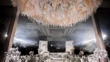 Salão de banquetes com assentos em níveis, centros de mesa florais e um candelabro.