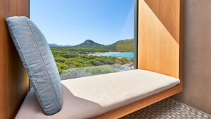 Quarto moderno com uma janela ampla que oferece vista para a paisagem costeira, um banco acolchoado e piso estampado.