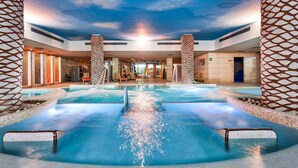 Uma grande piscina coberta com duas banheiras de hidromassagem, rodeada por espreguiçadeiras e um design arquitetônico moderno.