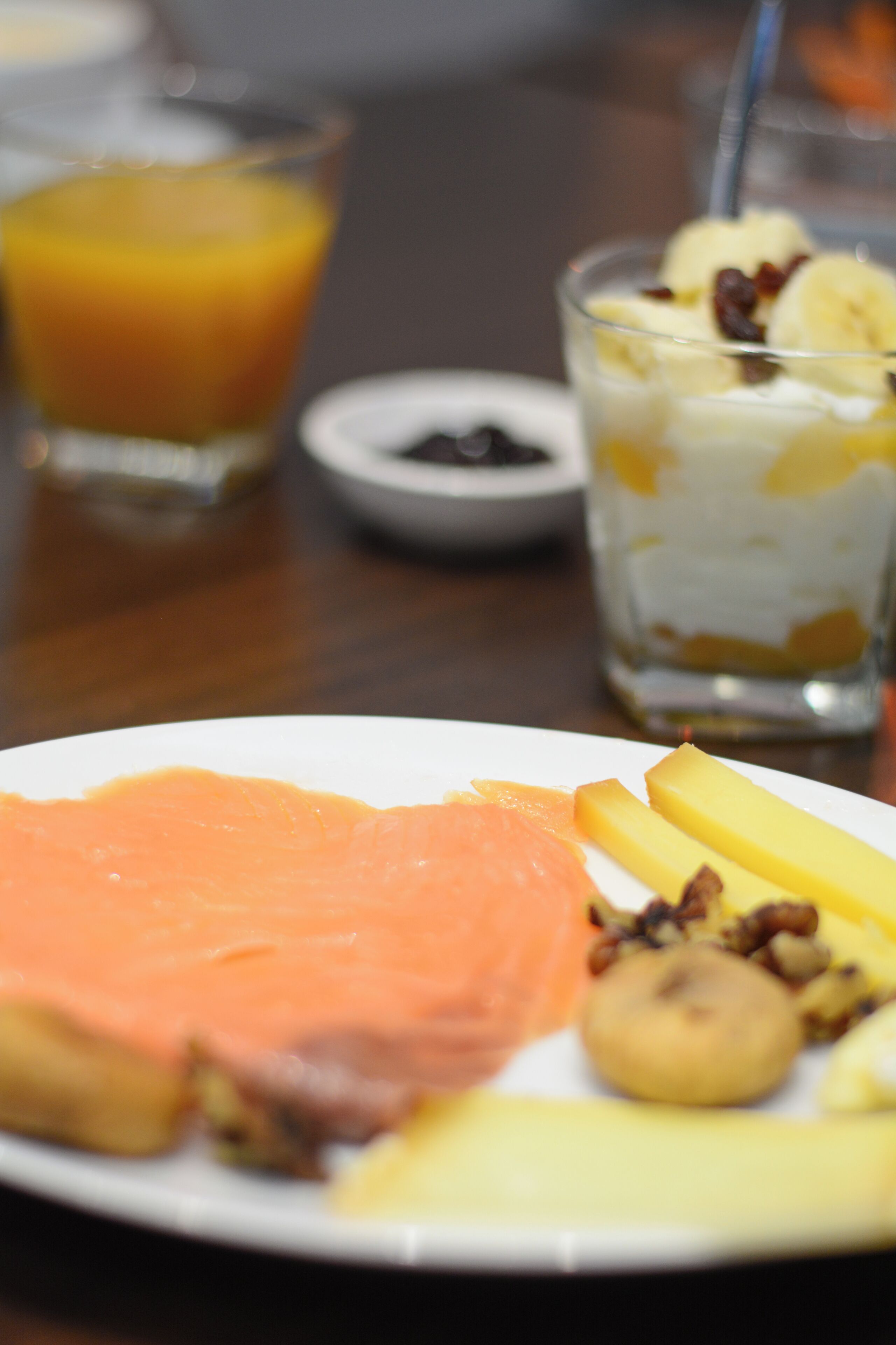 Um prato com salmão, abacaxi e nozes, e dois copos com suco de laranja e uma sobremesa.