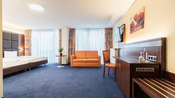 Quarto de hotel com cama, sofá, televisão e escrivaninha com abajur.