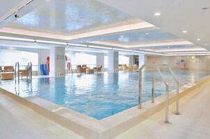 Piscina interna com água cristalina, rodeada por espreguiçadeiras e um solário.