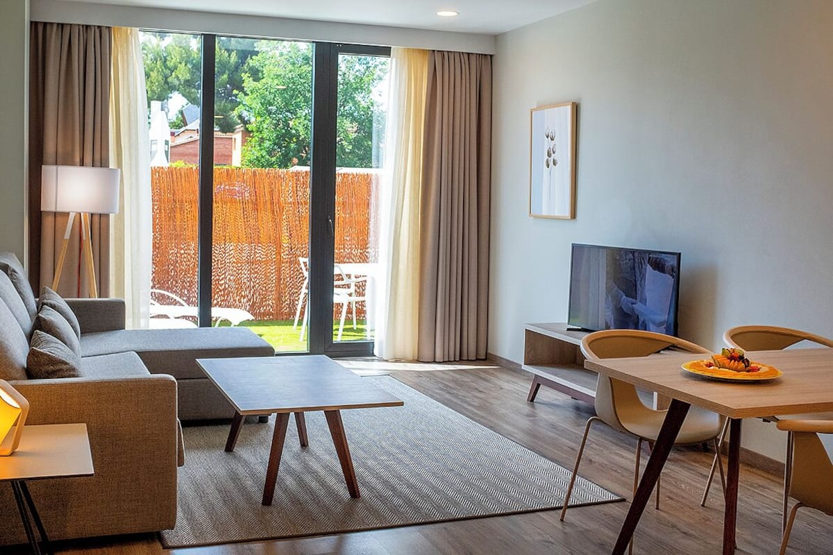 Uma sala de estar moderna com sofá, mesa de centro, mesa de jantar com cadeiras, TV e uma grande porta de vidro deslizante que dá para uma área externa.