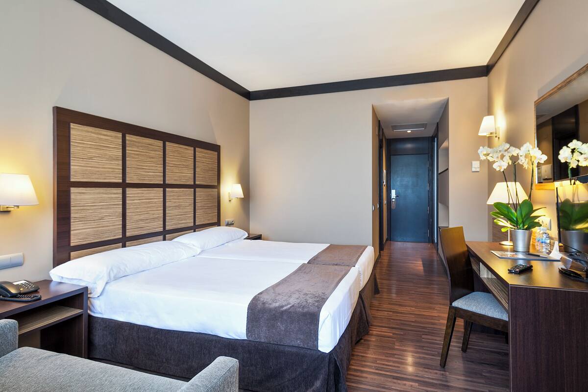 Quarto de hotel com uma cama grande, uma escrivaninha com cadeira, telefone e espelho.