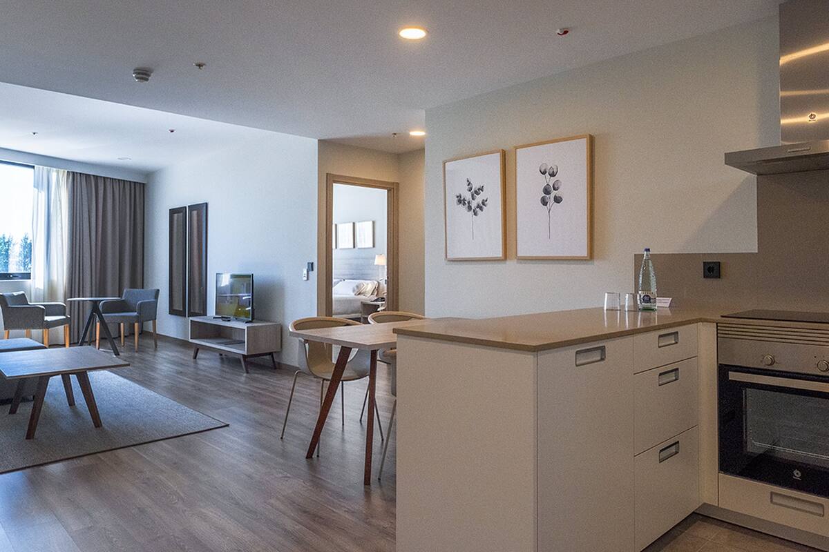 Uma cozinha moderna com forno embutido, sala de jantar com mesa e cadeiras, e sala de estar com sofá e televisão.