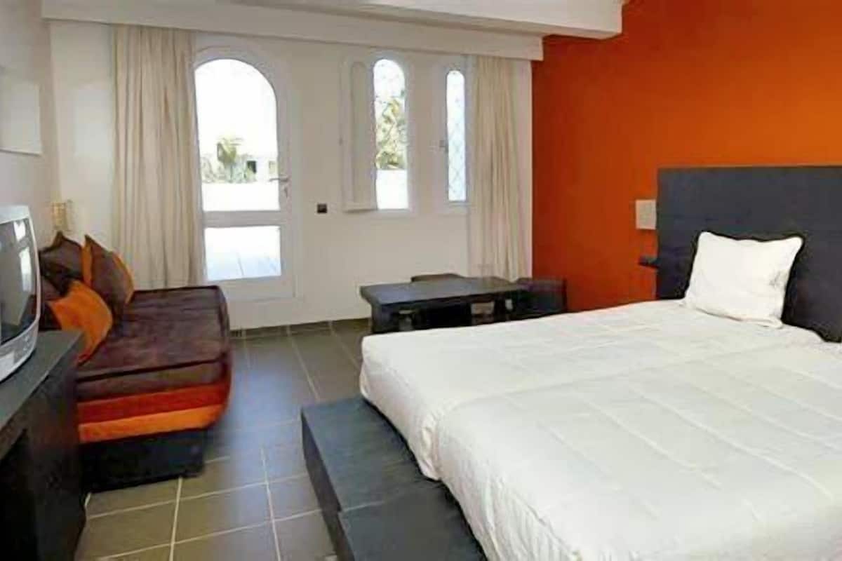 Quarto de hotel com cama, televisão e janela com cortinas.
