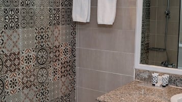 Um banheiro com ladrilhos estampados, uma banheira branca, uma pia com bancada de granito e um espelho.