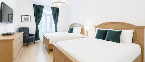 Quarto de hotel com duas camas, uma escrivaninha, uma cadeira, uma televisão e um candelabro.