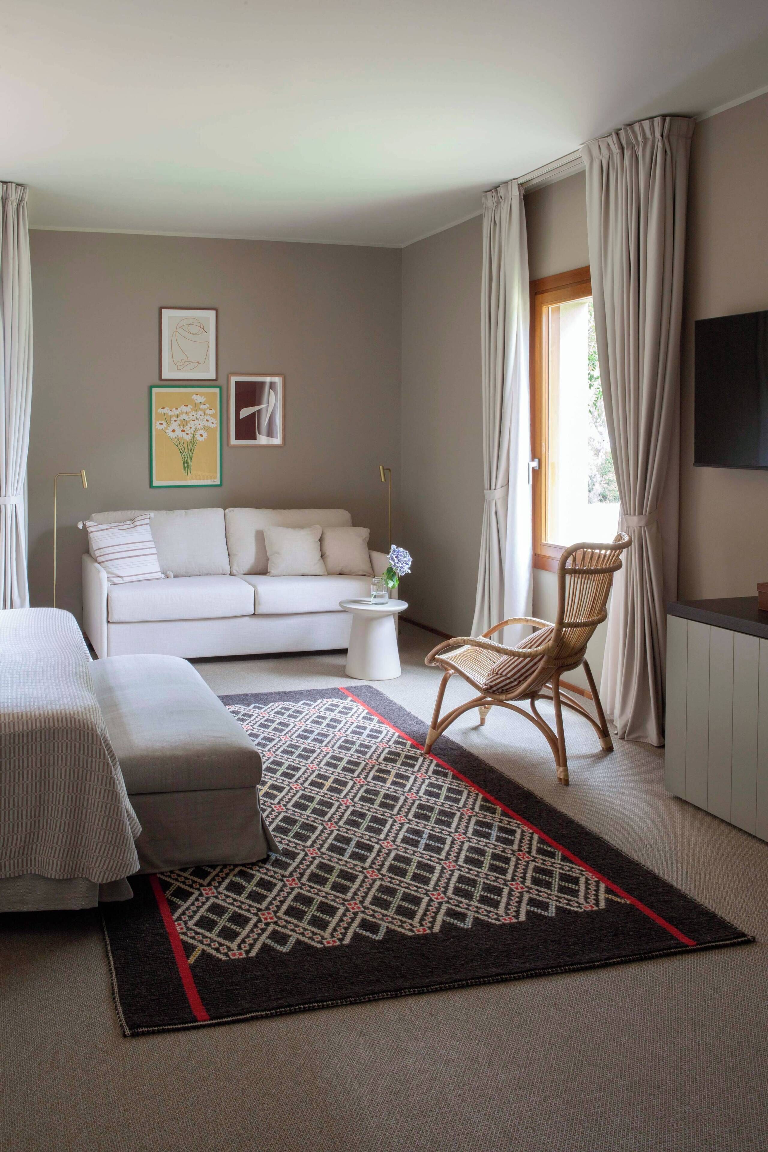 Quarto moderno com sofá branco, cadeira de vime, cama e televisão fixada na parede.