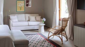Quarto moderno com sofá branco, cadeira de vime, cama e televisão fixada na parede.